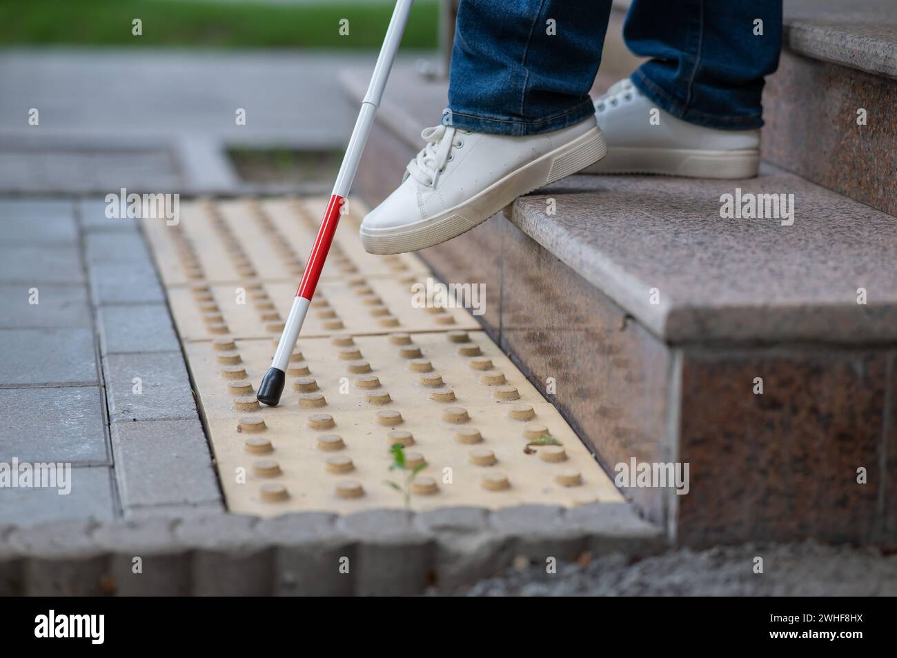 Close-up of female foot, walking stick and tactile tiles. Blind woman ...
