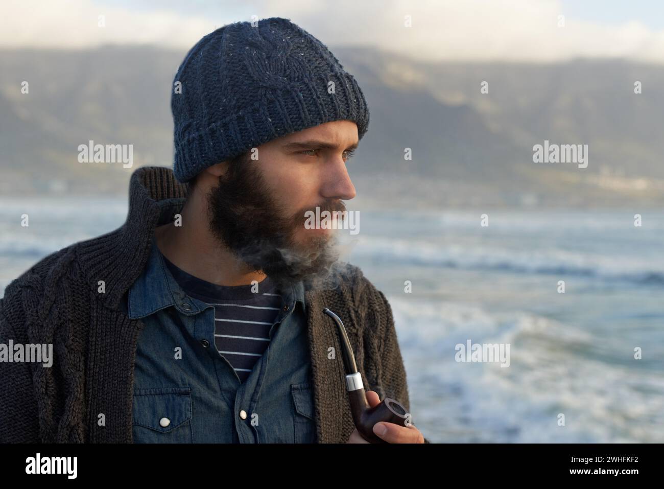 Beard, man and smoking a pipe by ocean, thinking and sailor habit on ...