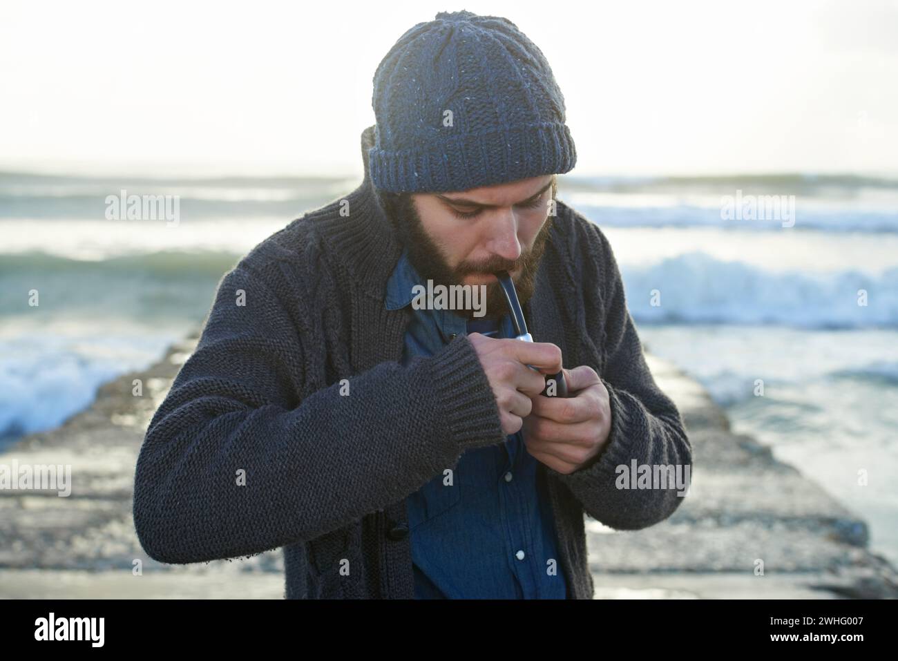 Bearded, man and smoking a pipe by ocean, lighter and tobacco habit on ...