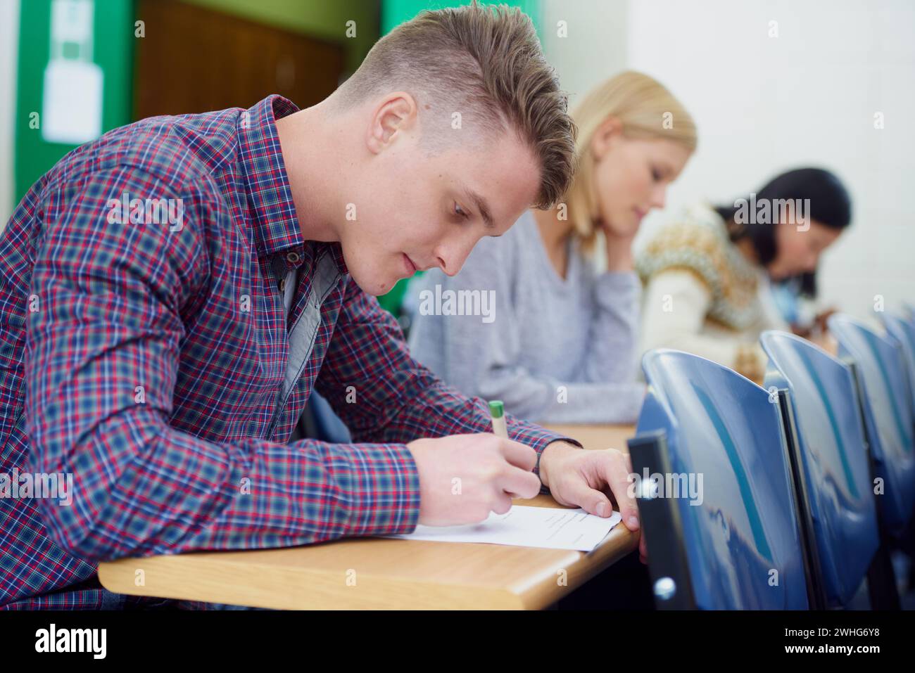 University student, desk and writing exam in classroom for education ...