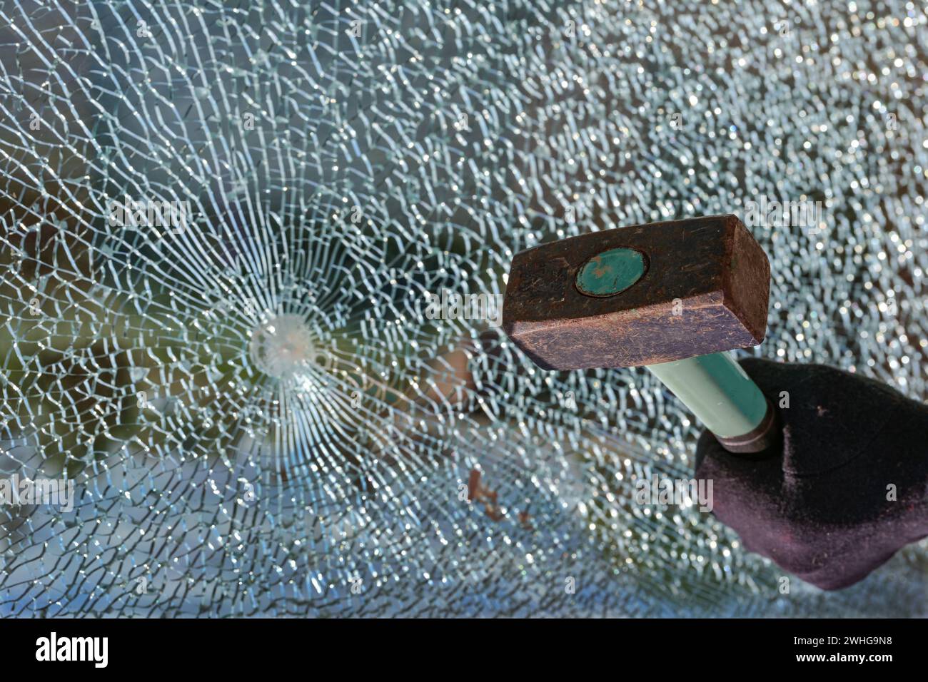 Hand with a hammer and a broken window made of safety glass, concept ...