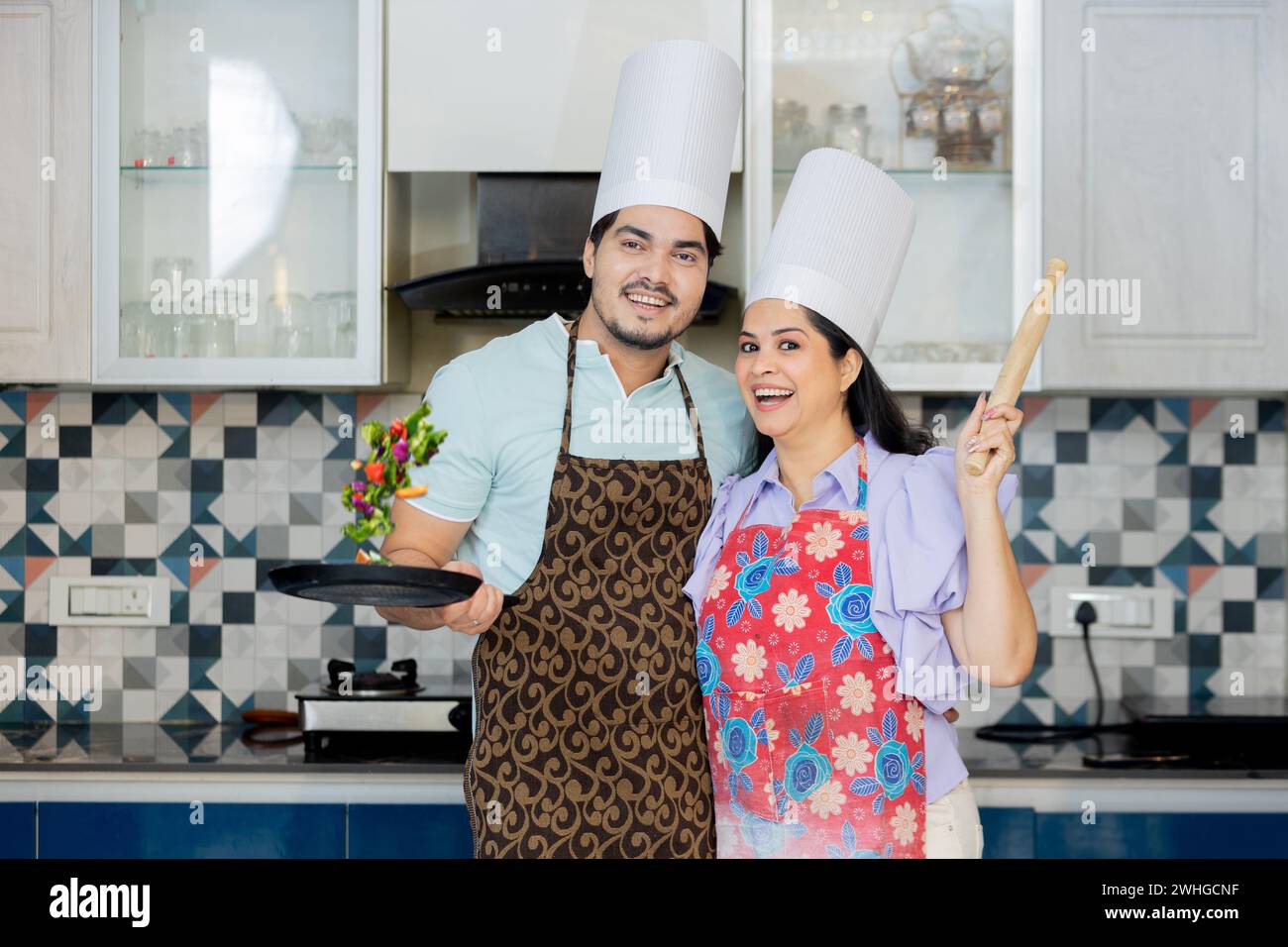 Happy indian couple dressed in cook uniform wearing a apron , chef hat ...