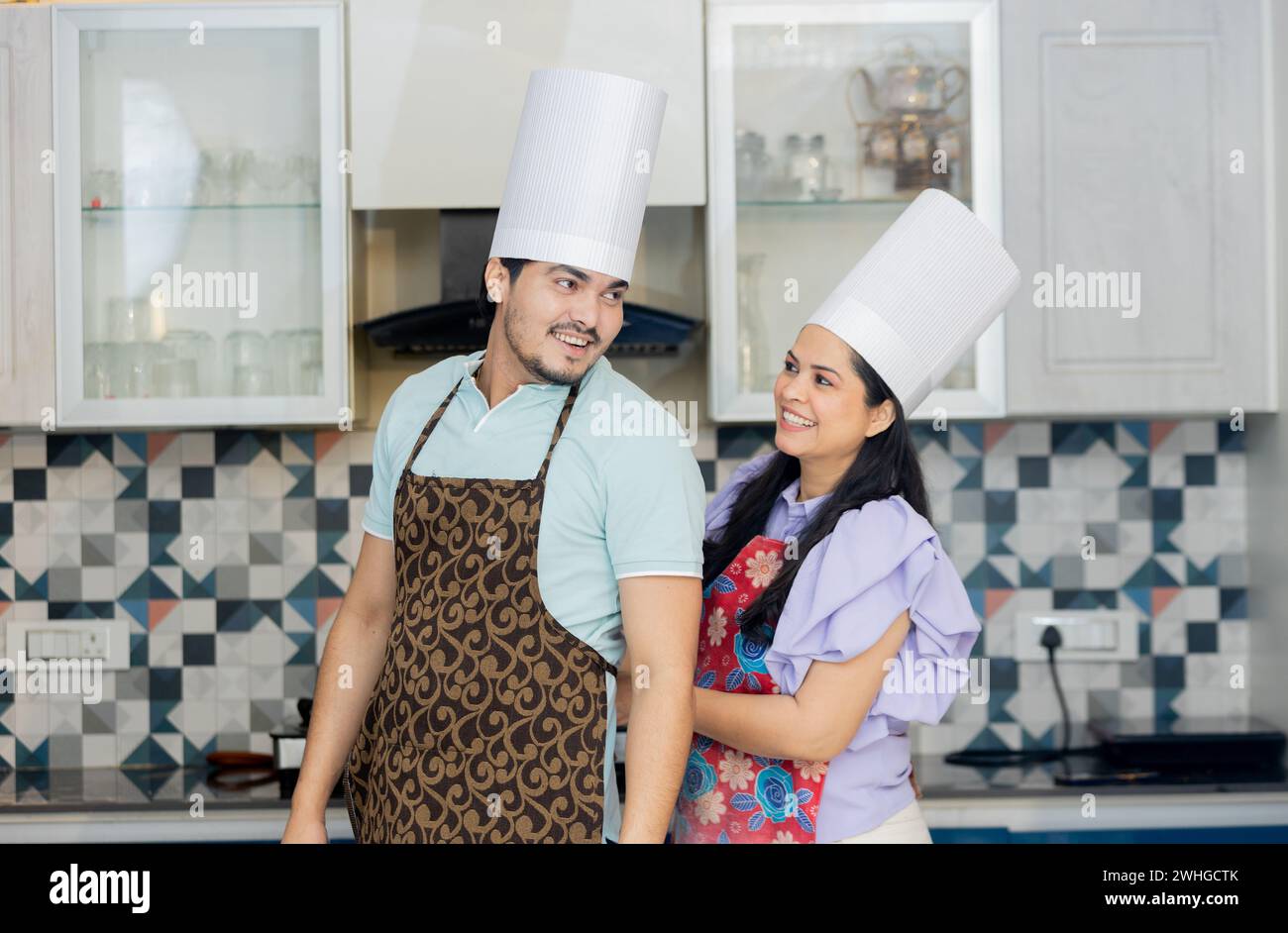 Happy indian couple dressed in cook uniform wearing a apron , chef hat ...
