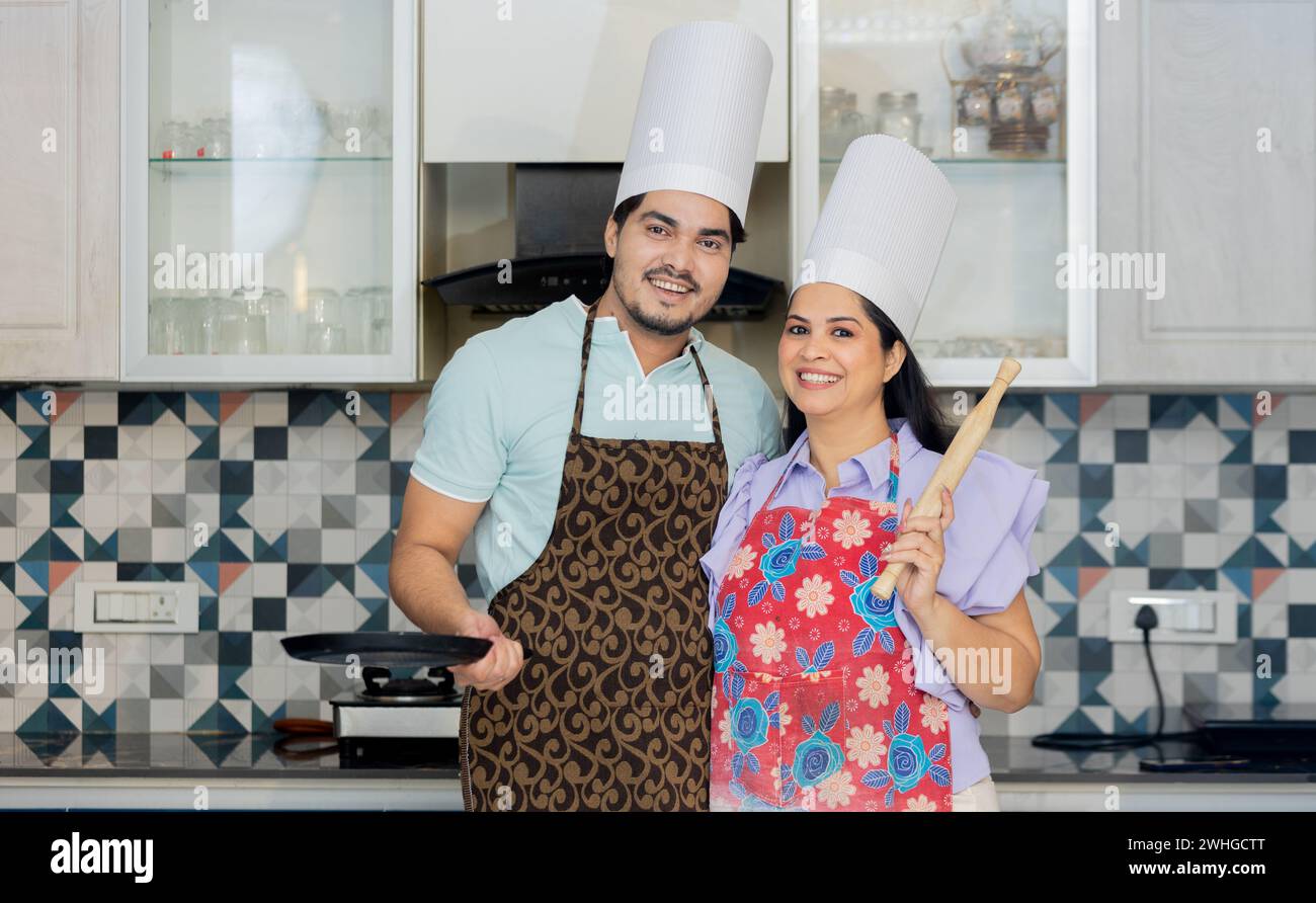 Happy indian couple dressed in cook uniform wearing a apron , chef hat ...