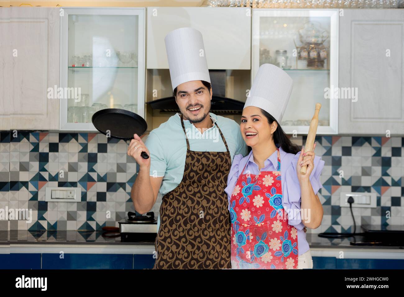 Happy indian couple dressed in cook uniform wearing a apron , chef hat ...
