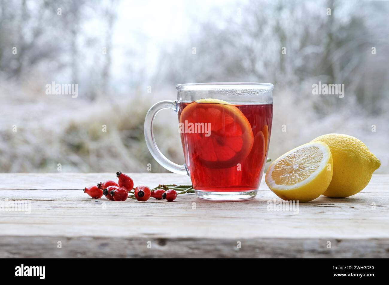 Hot tea from red rose hips with lemon slices in a glass mug outdoors on ...