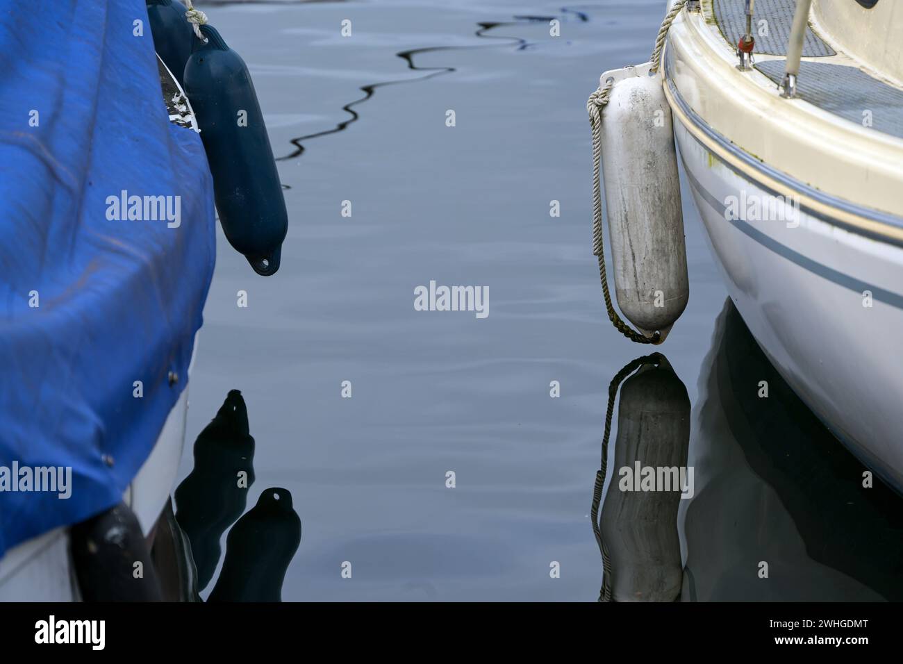 Two boats lying still side by side in the water with a blue and a white ...