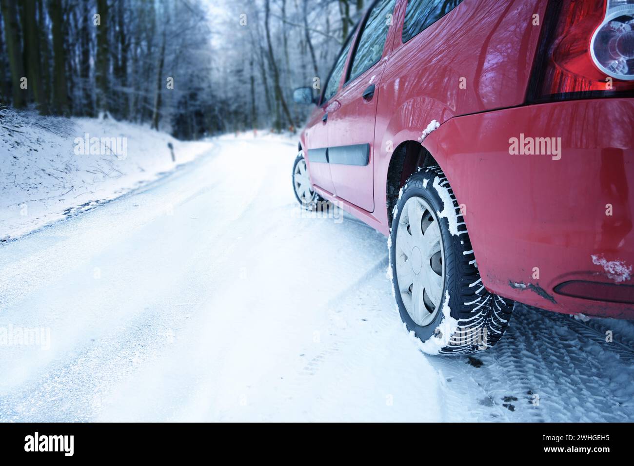 Red car driving on snow in winter on a curvy country road in a forest ...
