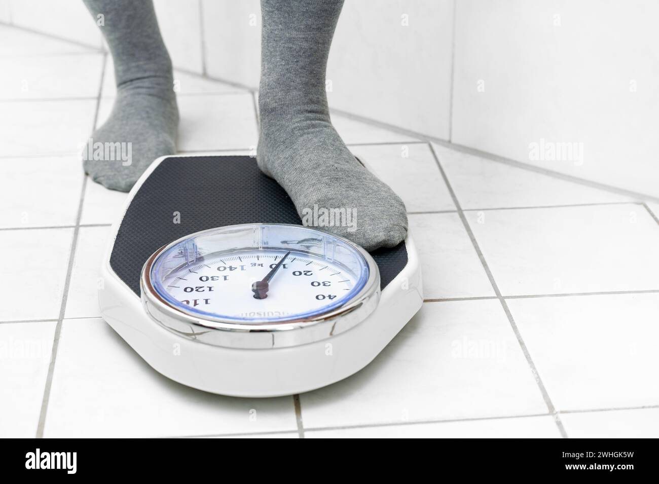 Feet in socks stepping on a personal scale on the tiled bathroom floor ...