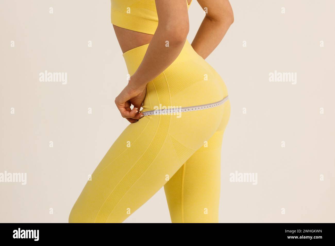 Sporty woman in yellow sport suit measures body with measuring tape ...