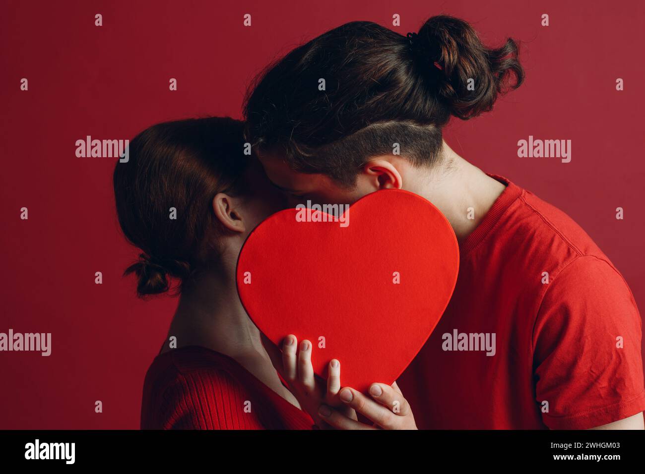 Man and woman young couple kissing and hiding behind heart-shaped box ...