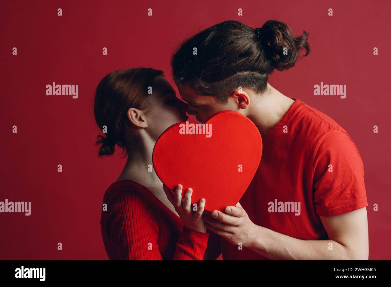 Man and woman young couple kissing and hiding behind heart-shaped box ...