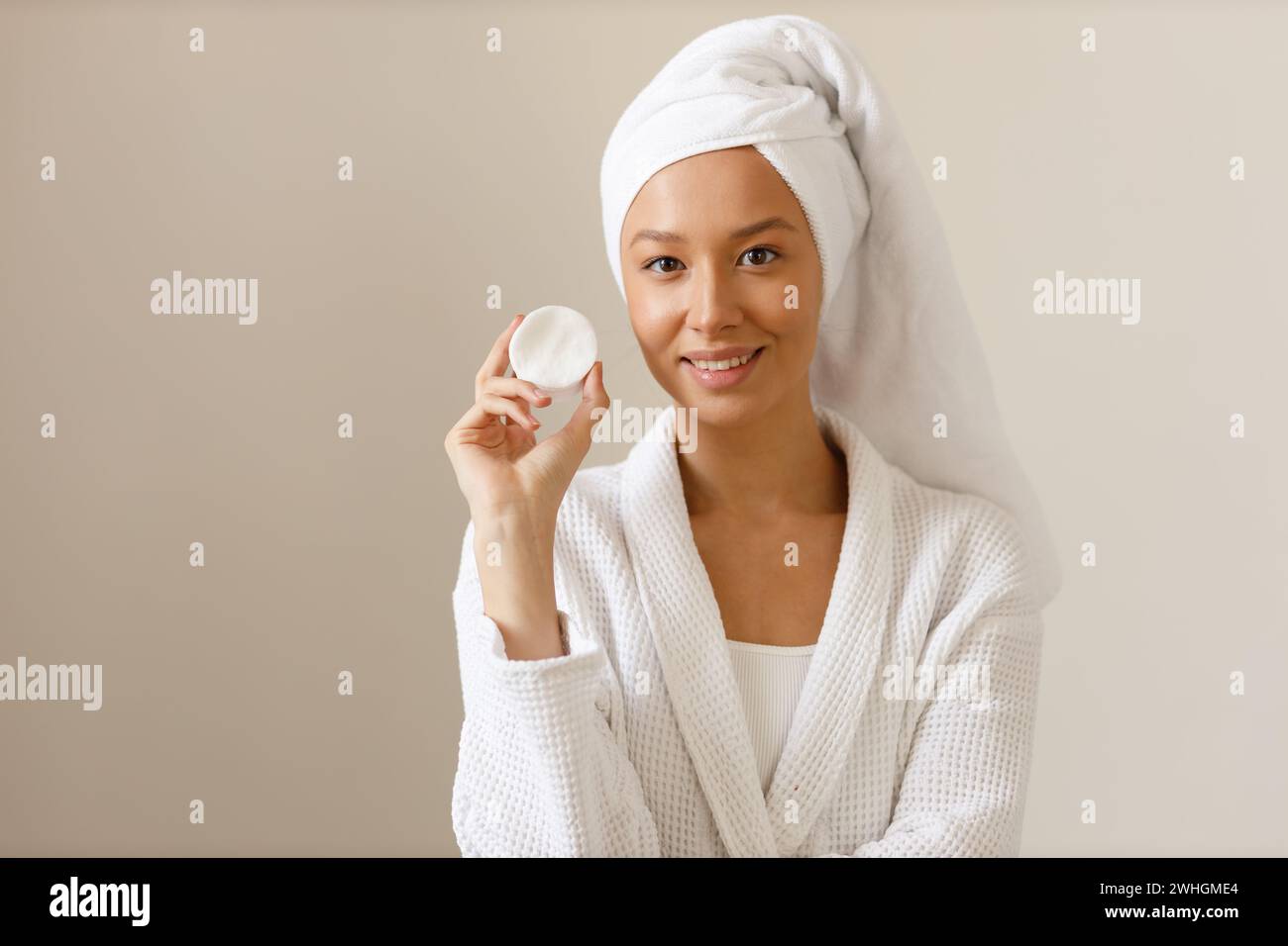 Young woman in white robe and towel on her head wipes the skin of her ...