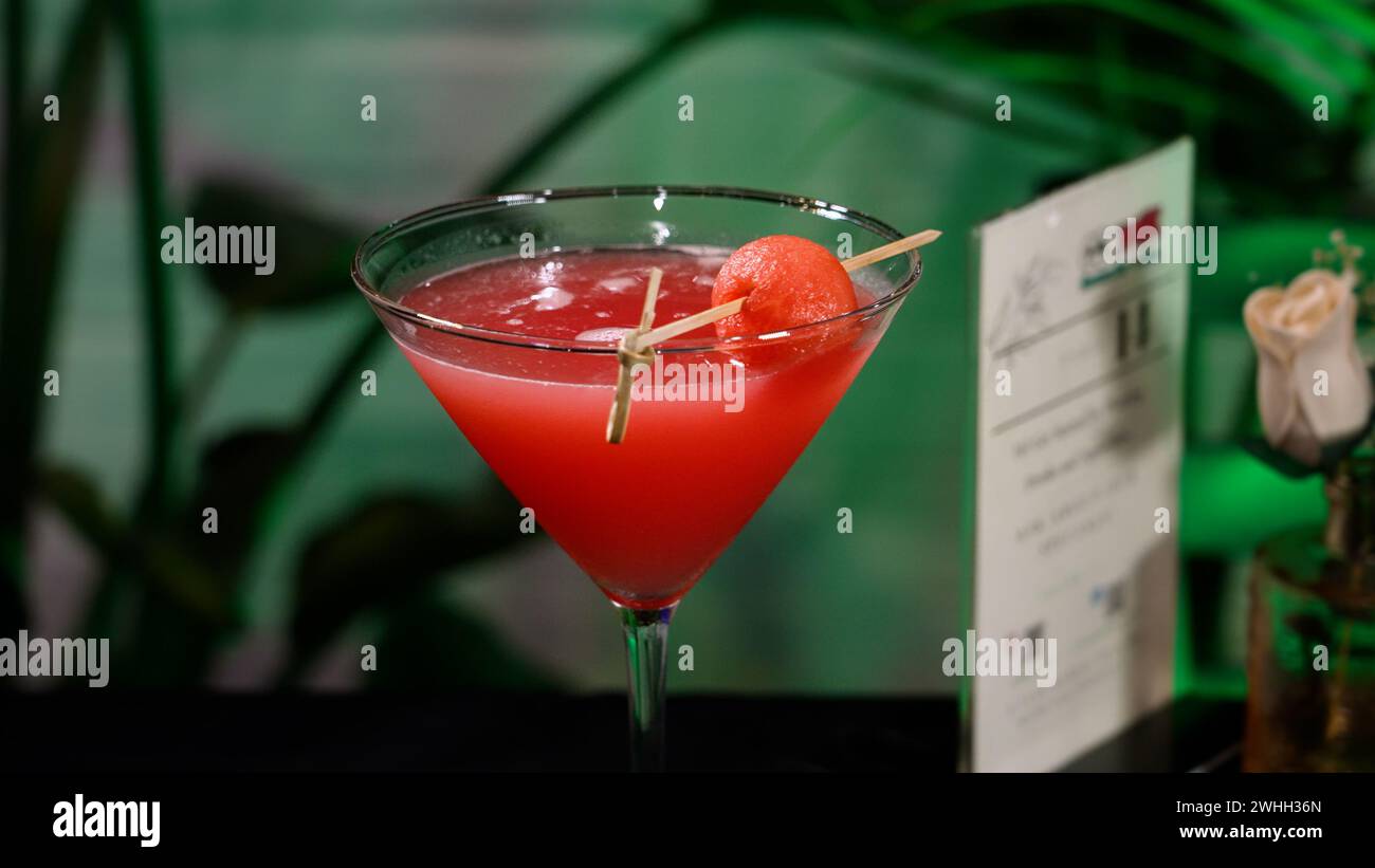 A close-up of a glass with a drink and a vibrant red berry garnish ...