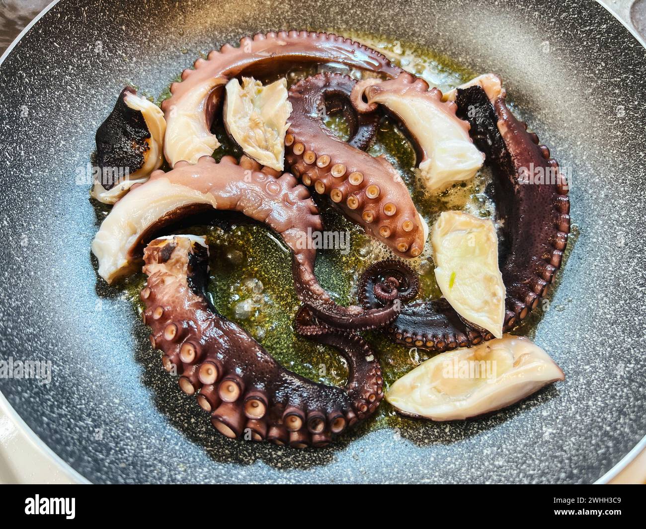 Pieces of octopus tentacles are fried in oil in a frying pan Stock ...
