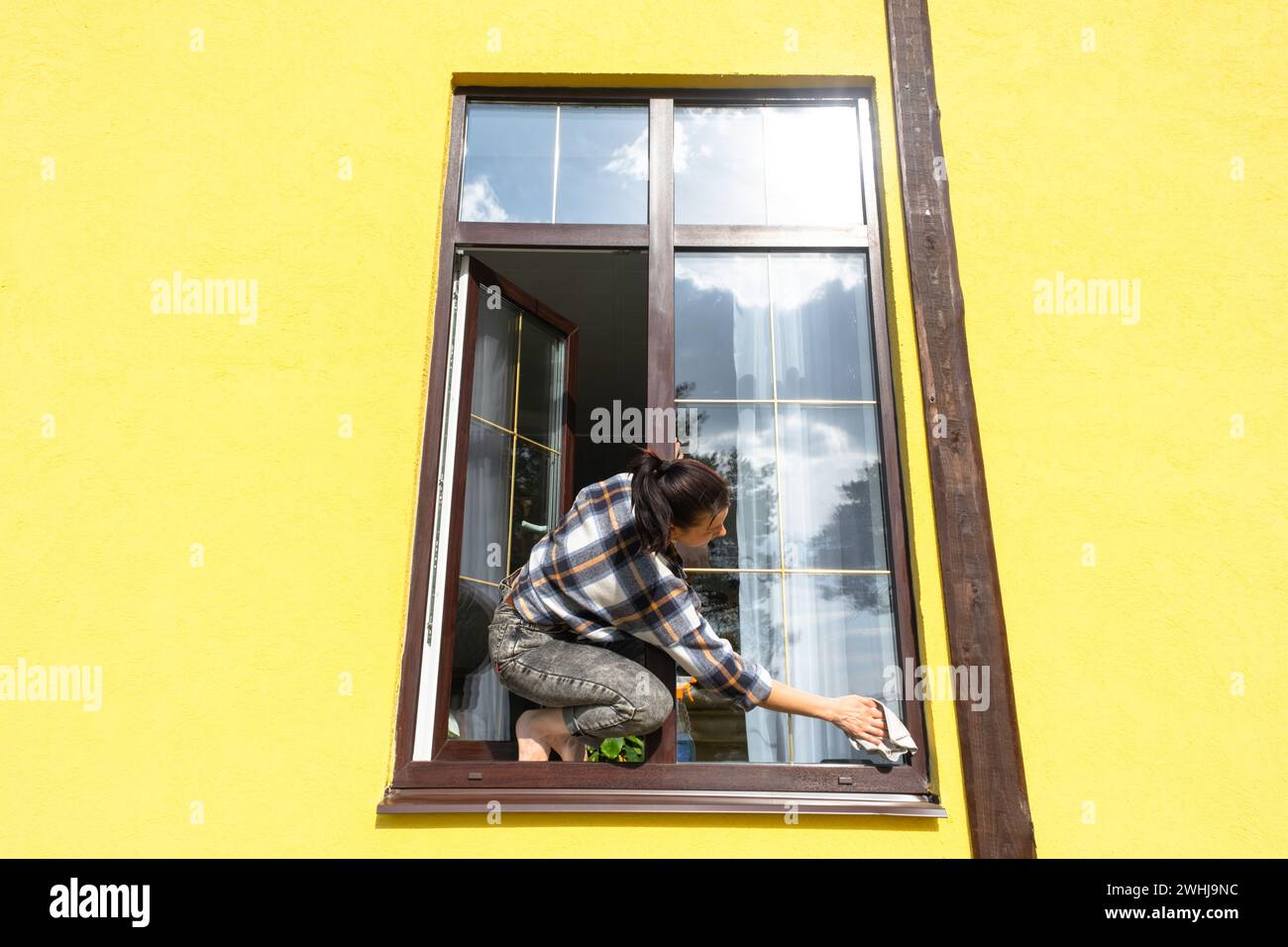 A woman manually washes the window of the house with a rag with a spray ...