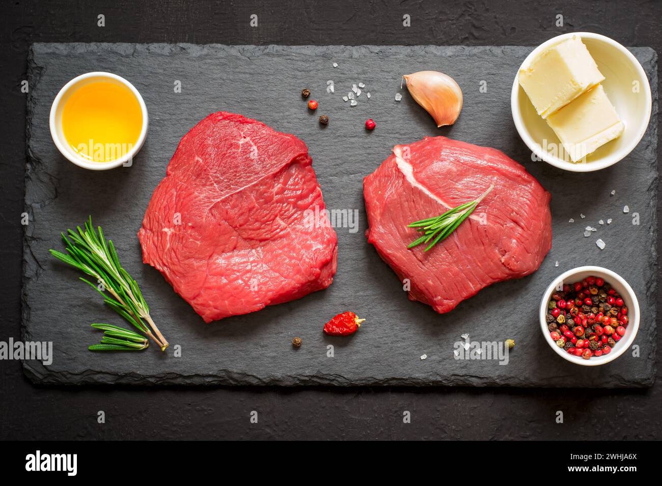 Raw beef steaks and rosemary on a black slate board. Top view Stock ...