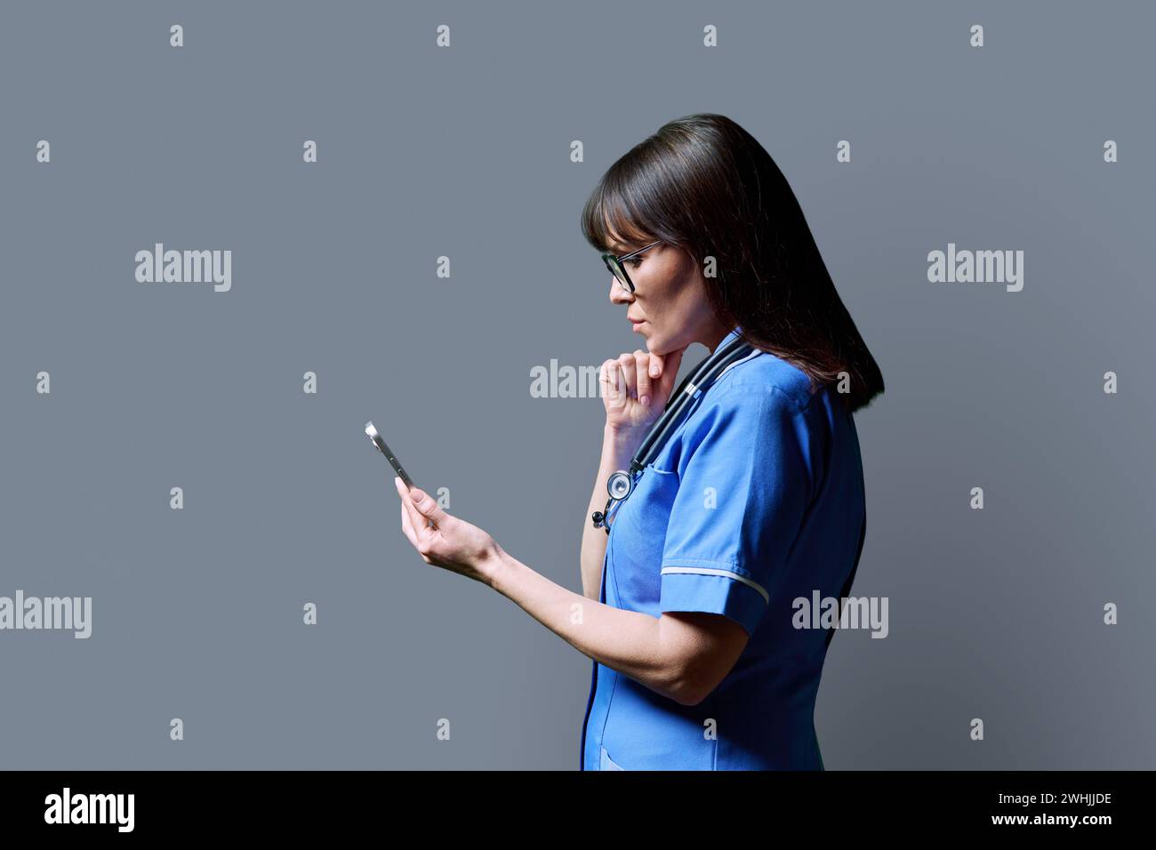 Female nurse using smartphone, profile view on gray studio background ...