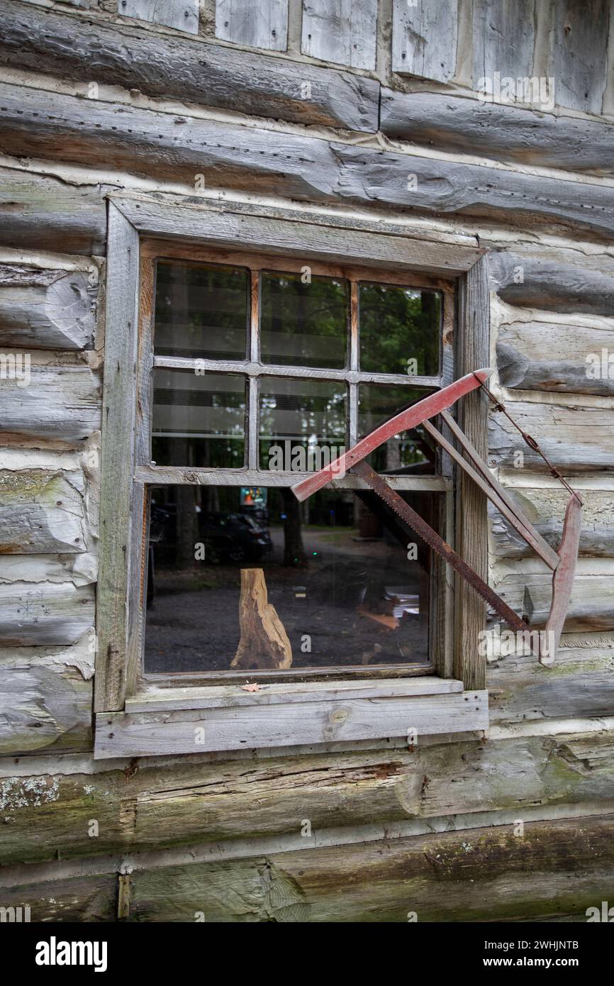 Side facade of a log farmhouse and window with old saw hanging, Ottawa ...