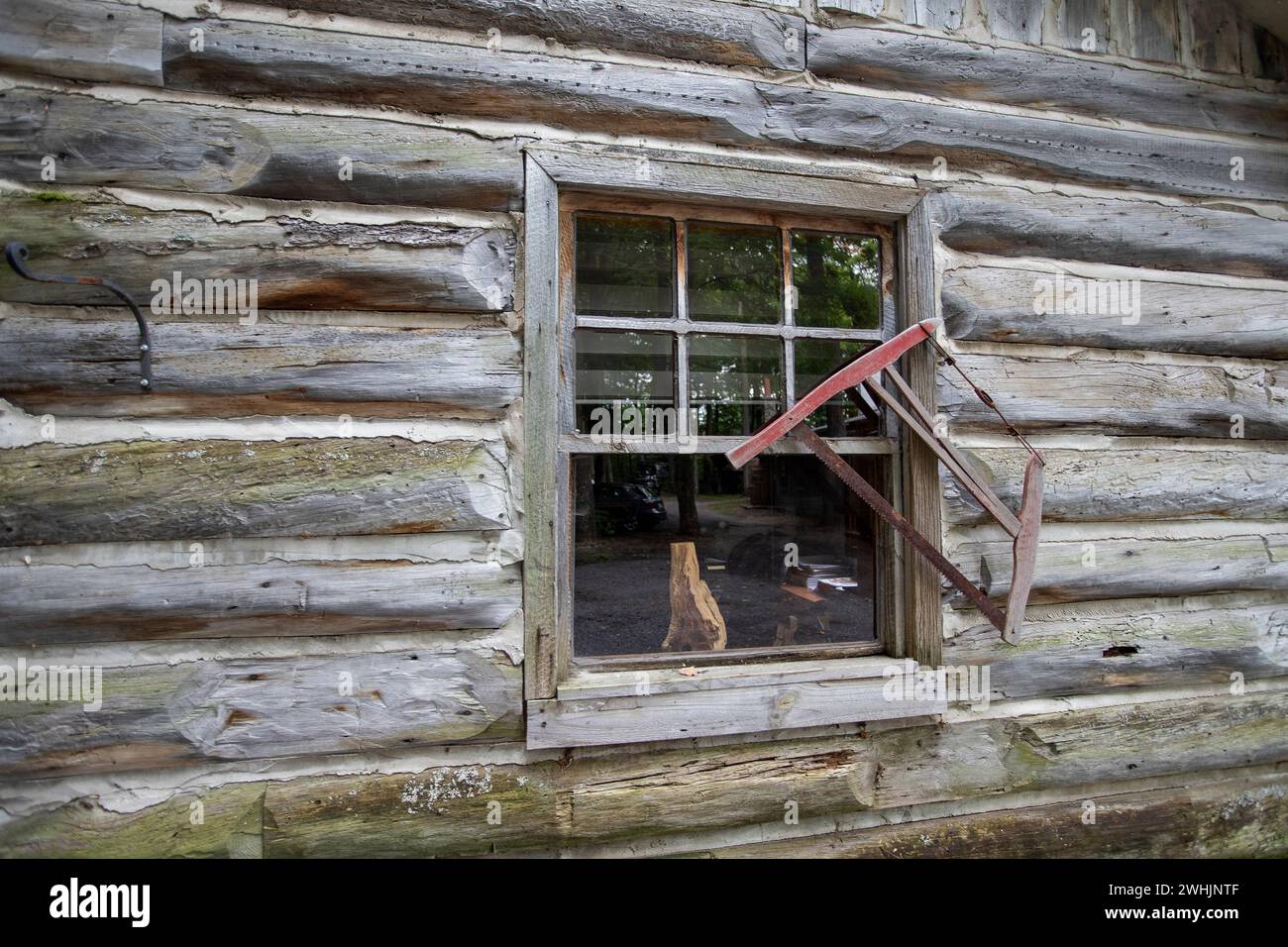 Side facade of a log farmhouse and window with old saw hanging, Ottawa ...