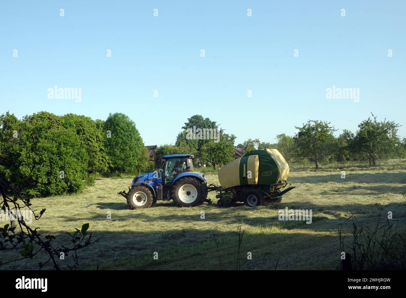 Farmer harvesting hay with a round baler Stock Photo - Alamy