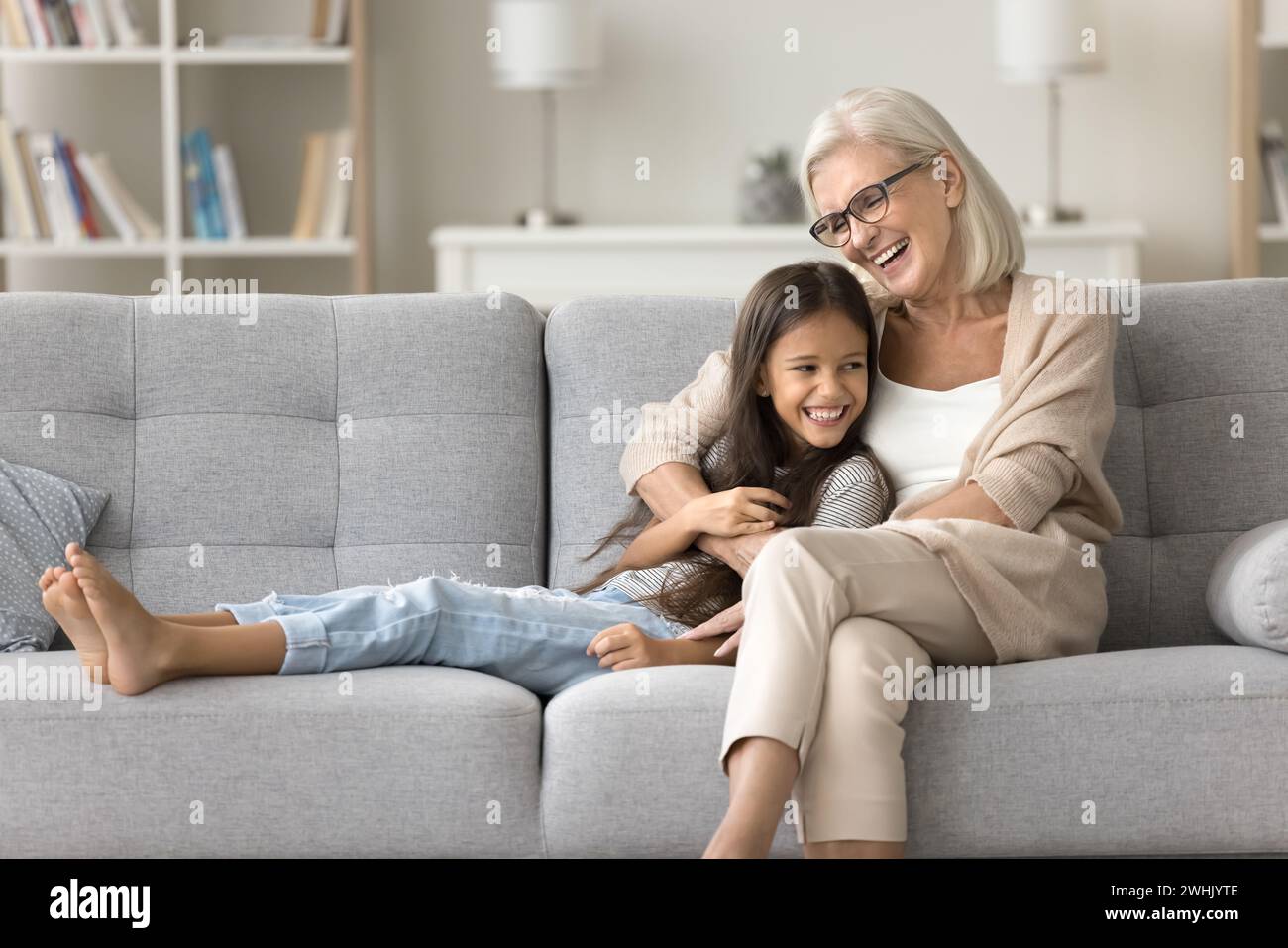 Cheerful grandma and happy pretty granddaughter kid resting on sofa ...