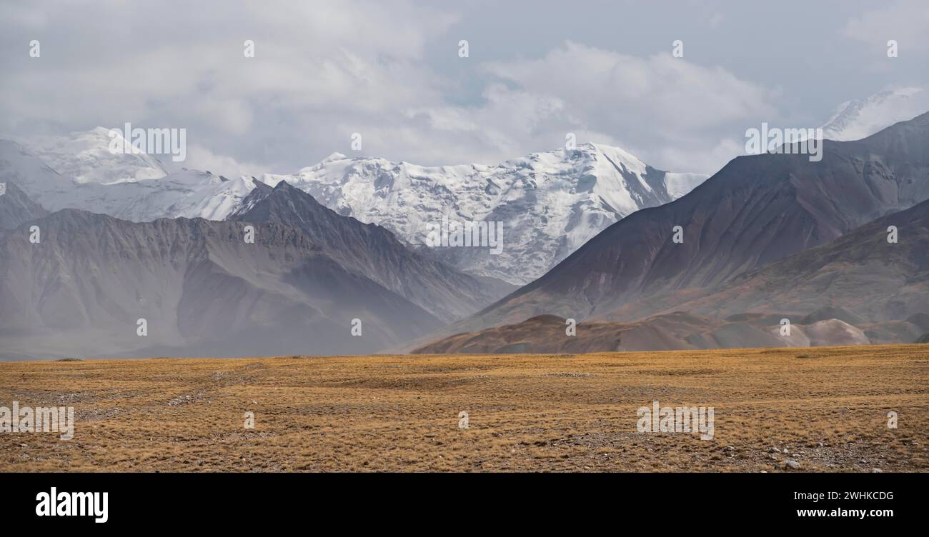 Glaciated, cloud-covered mountain peaks and golden meadows, Lenin Peak ...