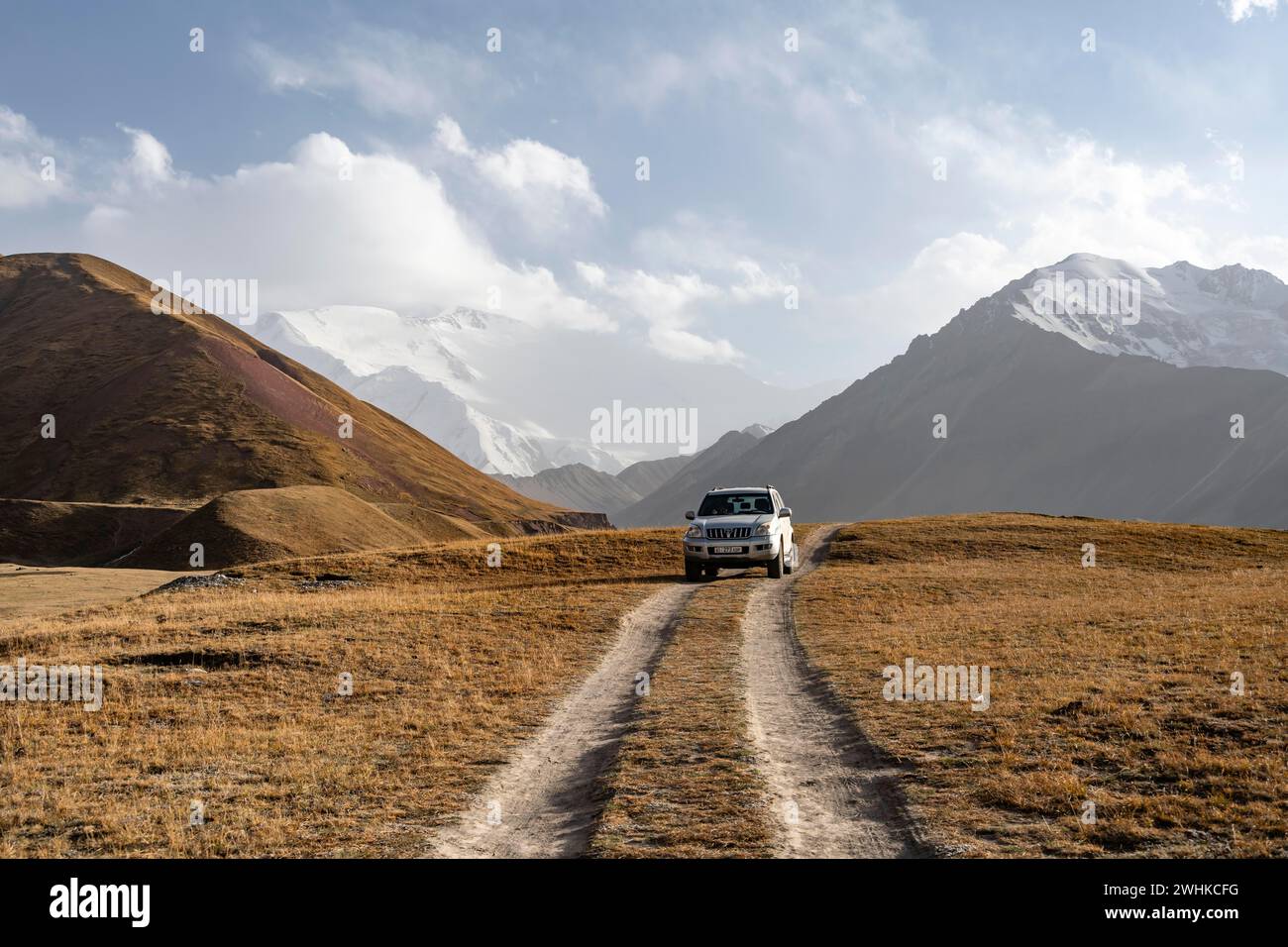 Off-road vehicle on a track between yellow meadows, glaciated high ...