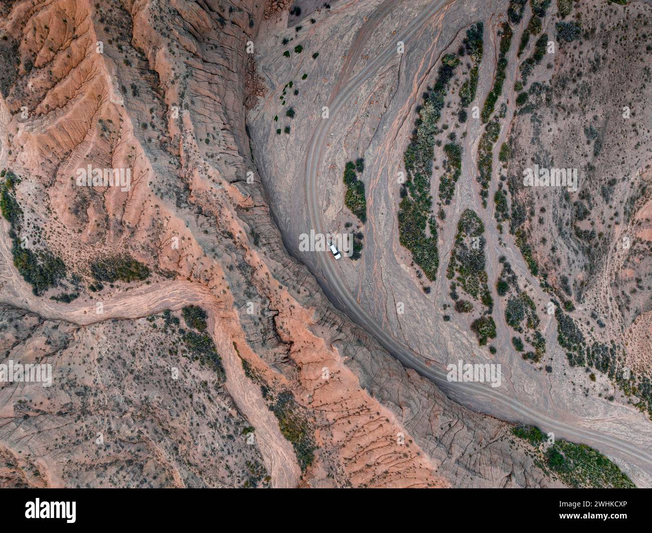 Off-road vehicle on a track in a riverbed, landscape of eroded hills ...