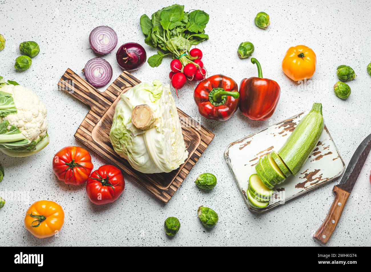Fresh various vegetables with wooden cutting boards and knife on white kitchen table top view ...