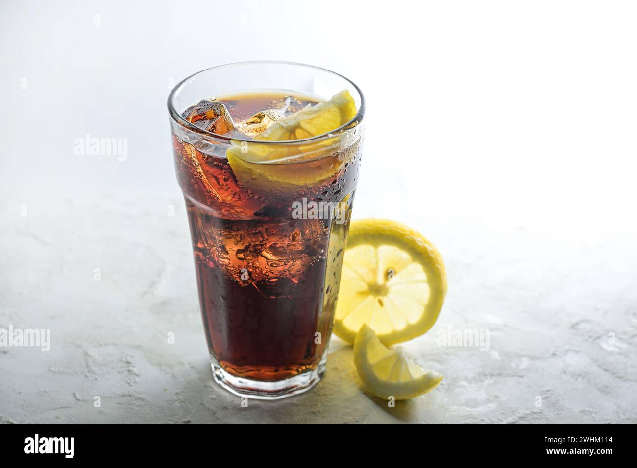 Fresh cola with ice cubes and lemon slices in a drinking glass, sweet ...