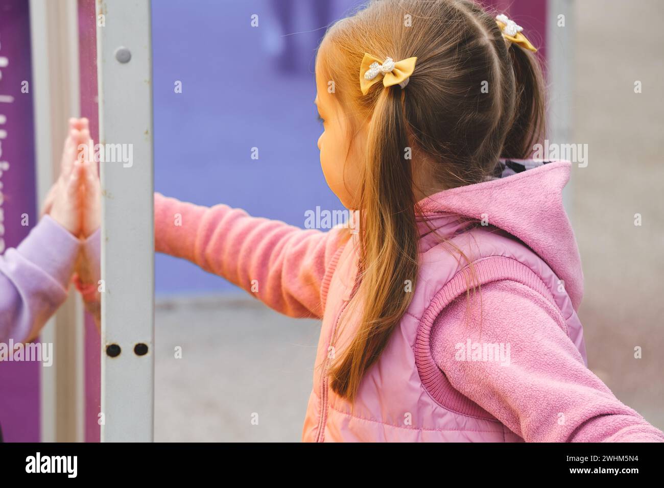 Child touching somebodies hand through glass wall outdoors. Girl making ...