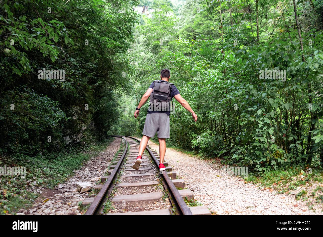 one young male tourist walks on the railway in the jungle of thailand ...