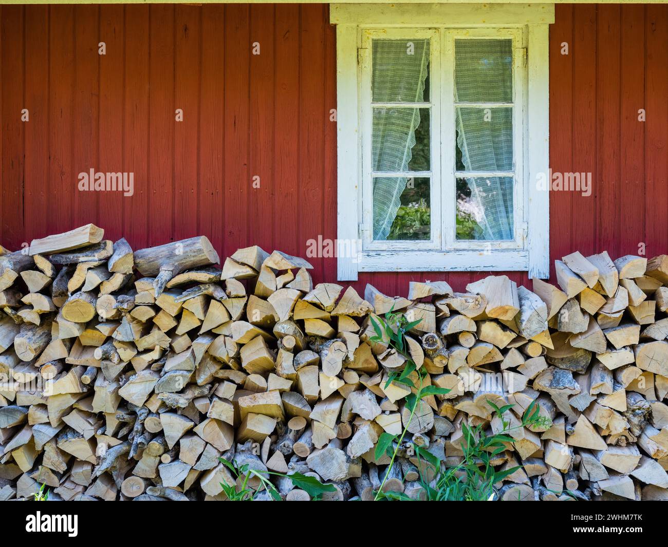 Traditional window and red painted wooden wall on a cabin. Fire wood is ...