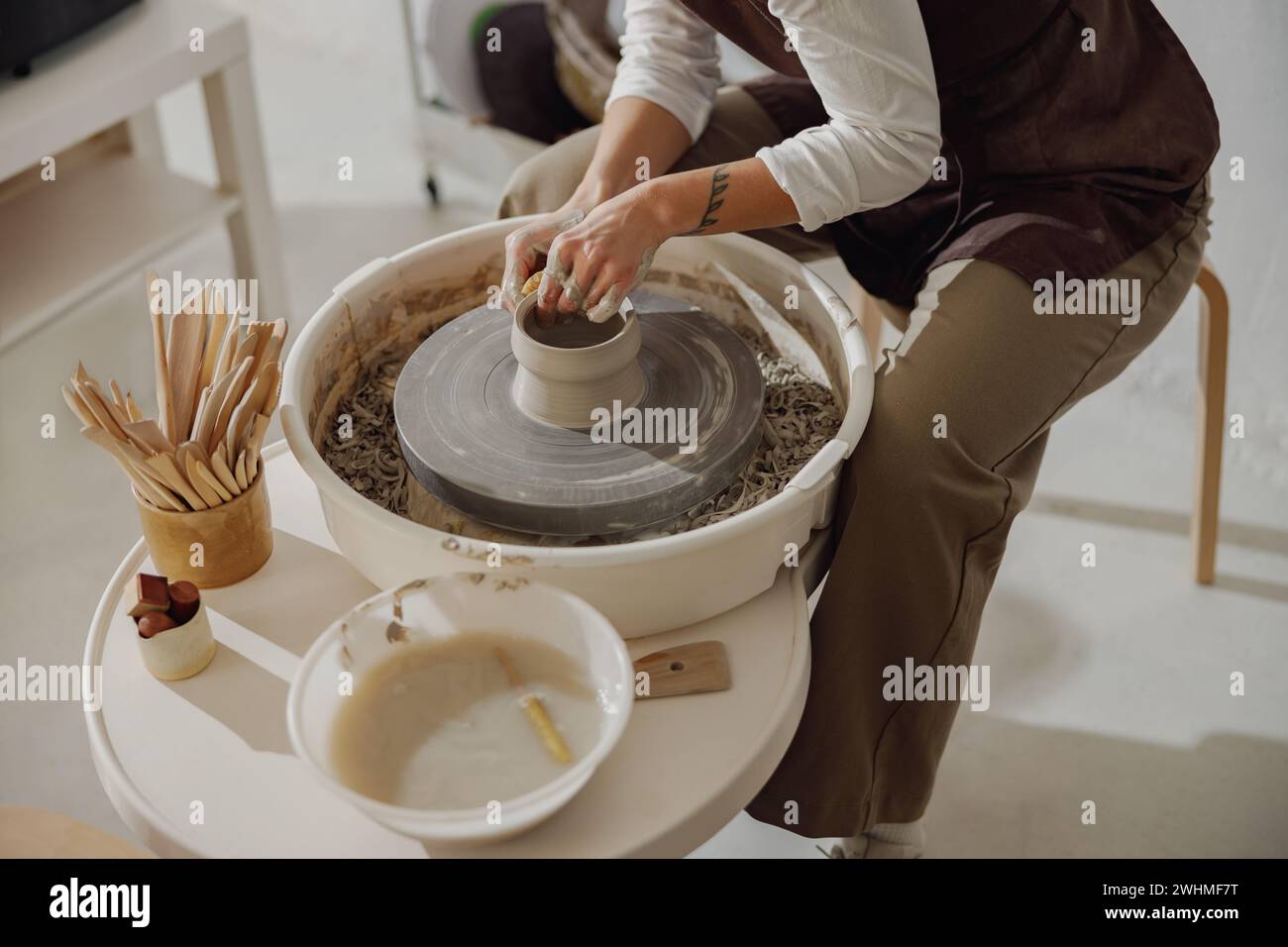 Female potter in apron making shape of clay vase on spinning pottery ...