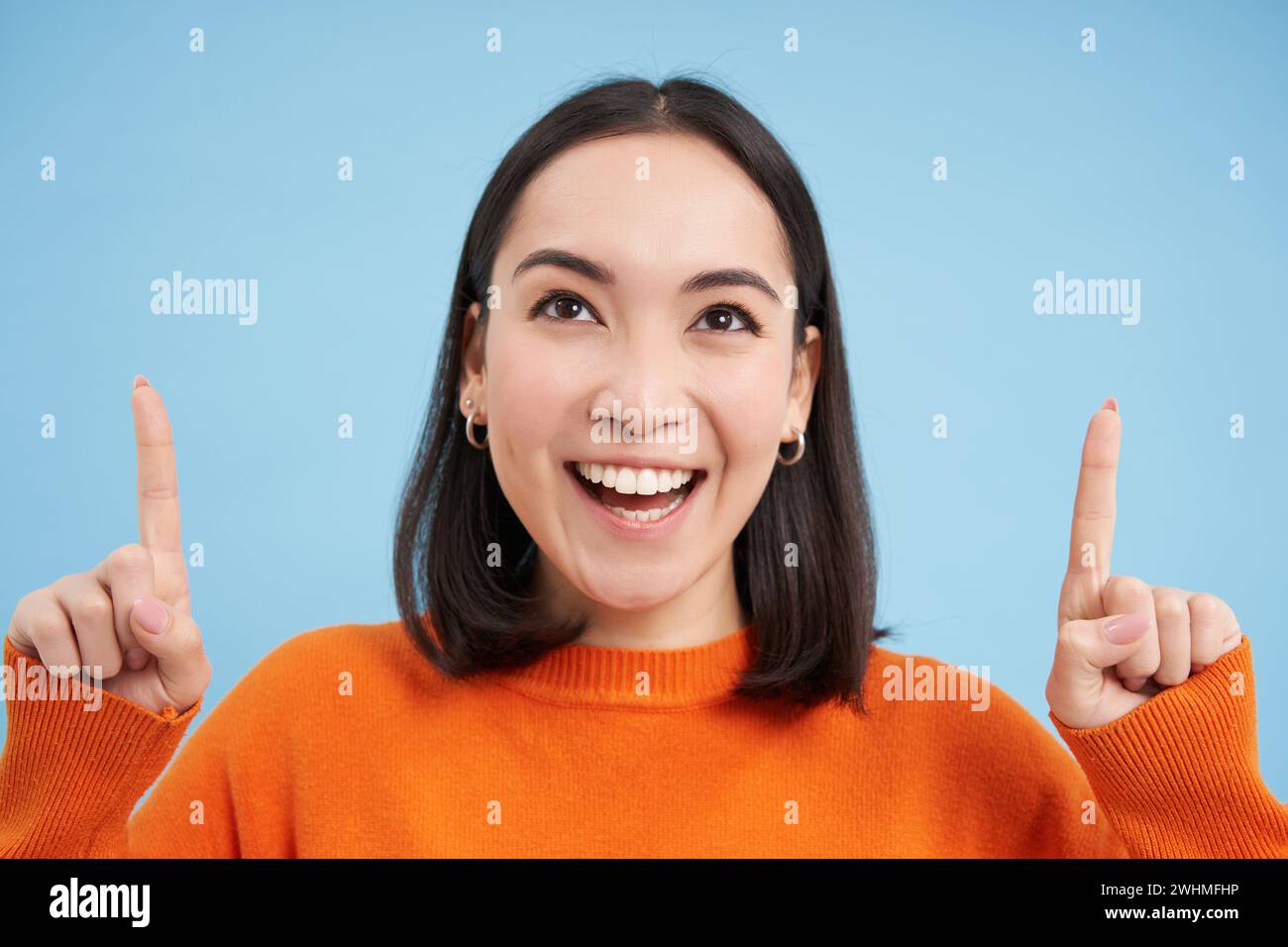 Beautiful asian girl points fingers up, shows banner on top ...