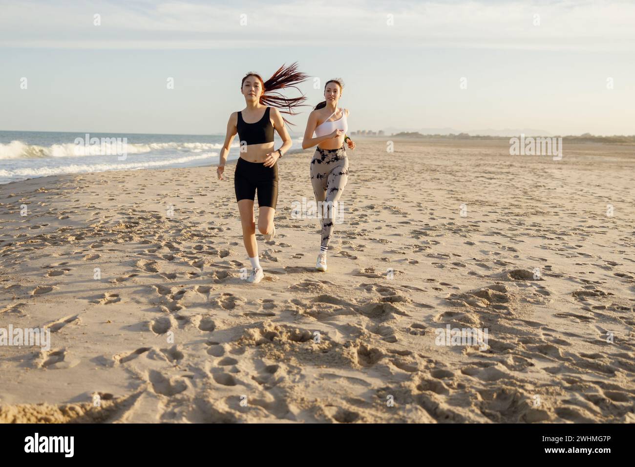 Young female friends in sportswear running on beach in morning sunrise ...