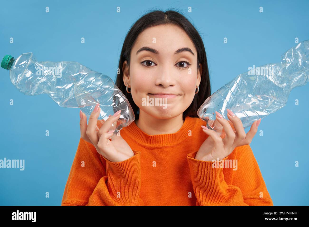 Cute korean woman shows two plastic bottles and smiles, recycles, sorts ...