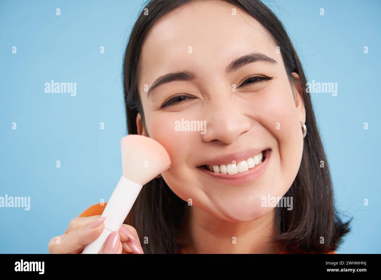Portrait of cheerful korean girl smiles, puts on makeup with brush ...