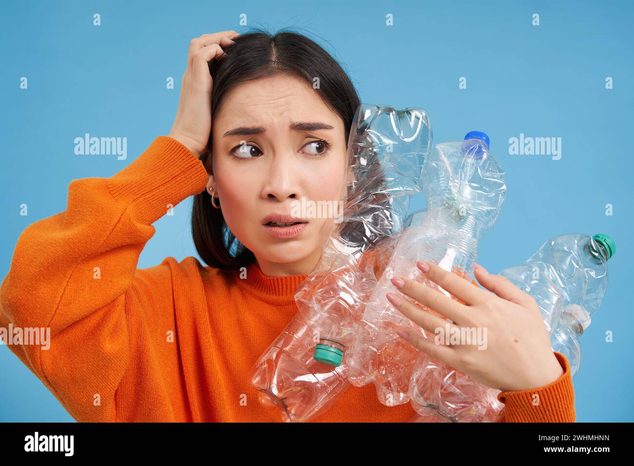 Portrait of asian girl with scared face, holding piles of plastic ...