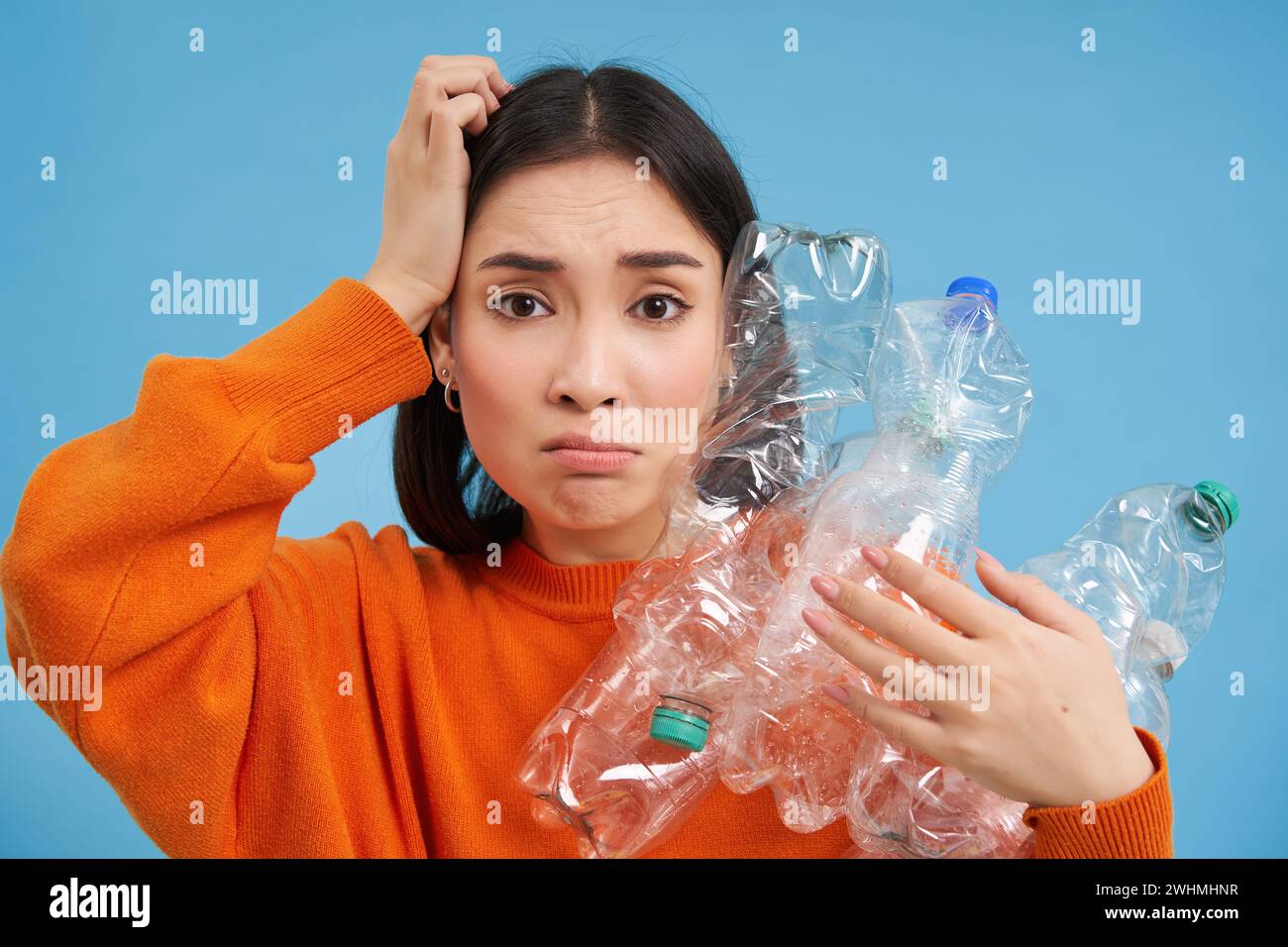Sad asian woman holding plastic bottles, looking troubled and upset ...