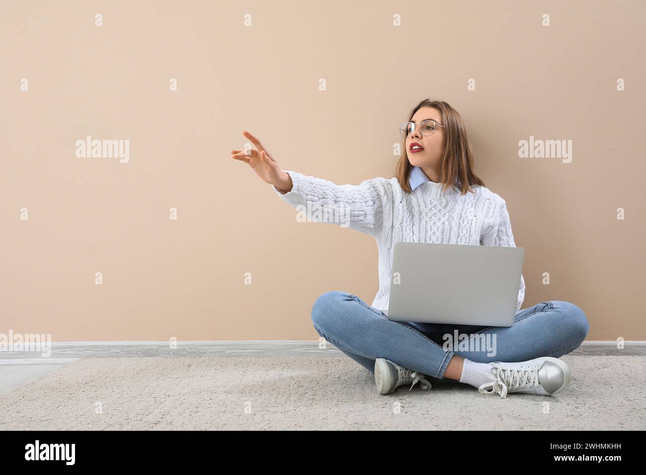 Female programmer with laptop sitting near beige wall Stock Photo - Alamy