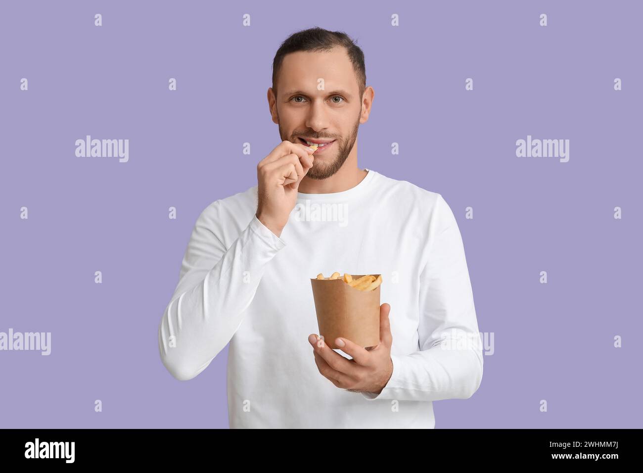 Young man eating french fries on purple background Stock Photo - Alamy