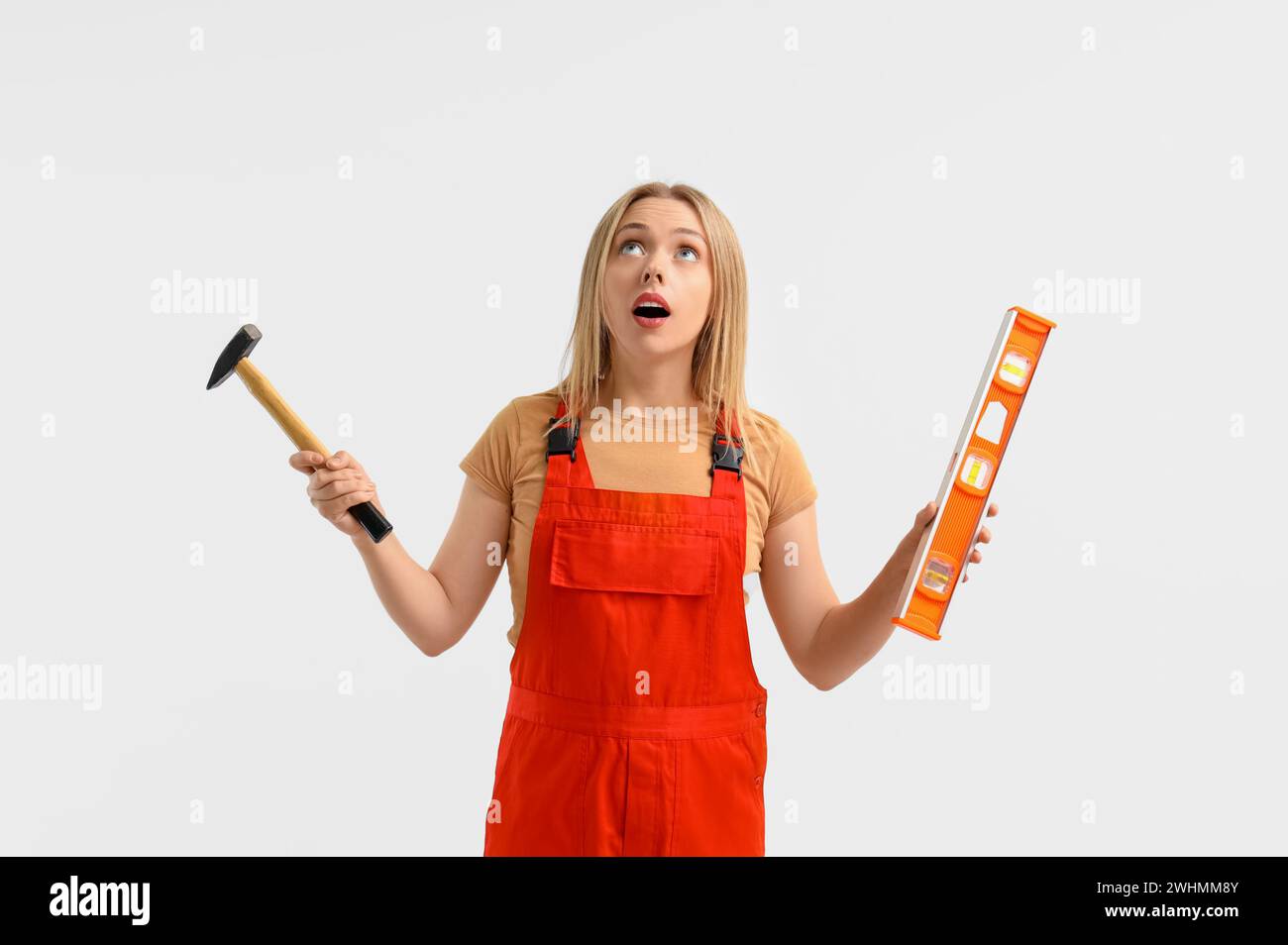 Surprised female builder with level and hammer on light background ...