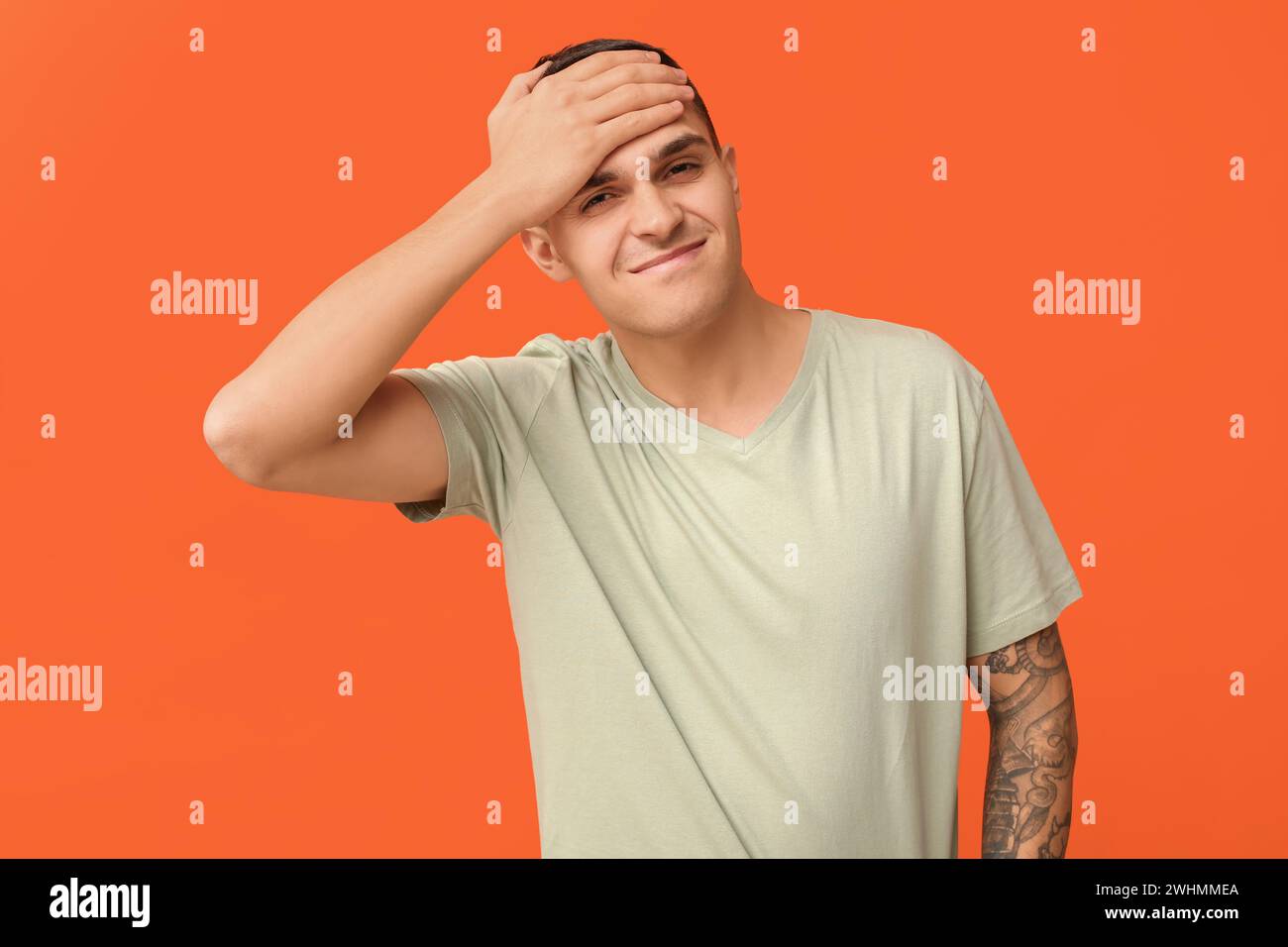 Handsome ashamed young man covering face with hand on orange background ...