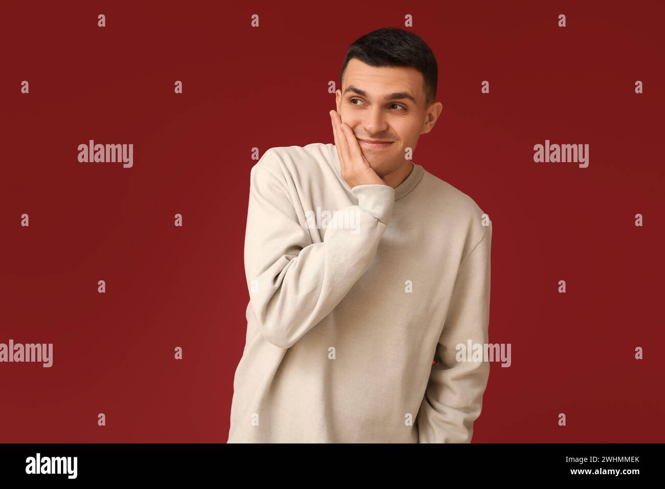 Handsome ashamed young man covering face with hand on red background ...