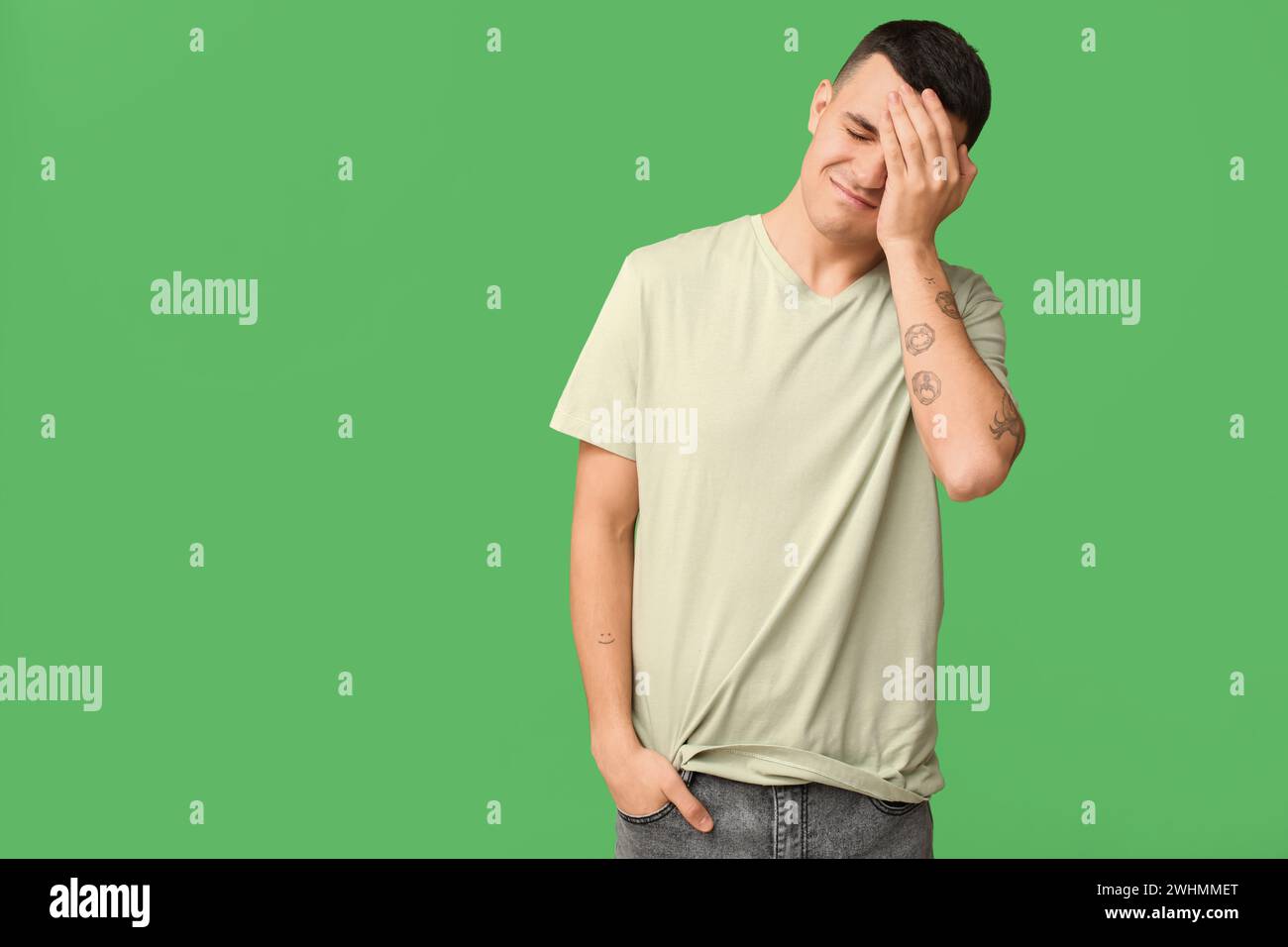 Handsome ashamed young man covering face with hand on green background ...