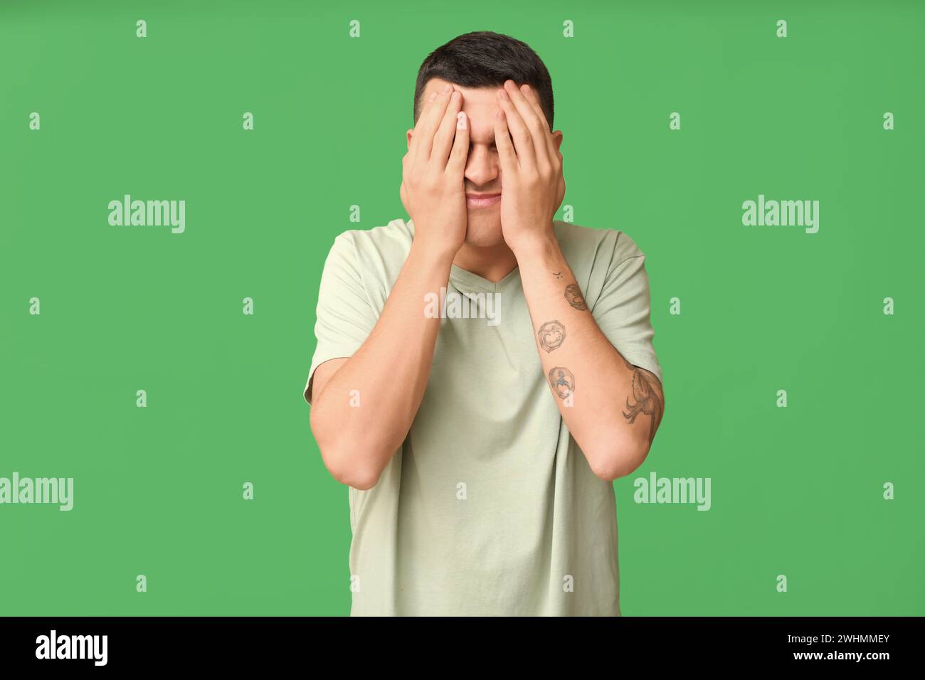 Handsome ashamed young man covering face with hands on green background ...