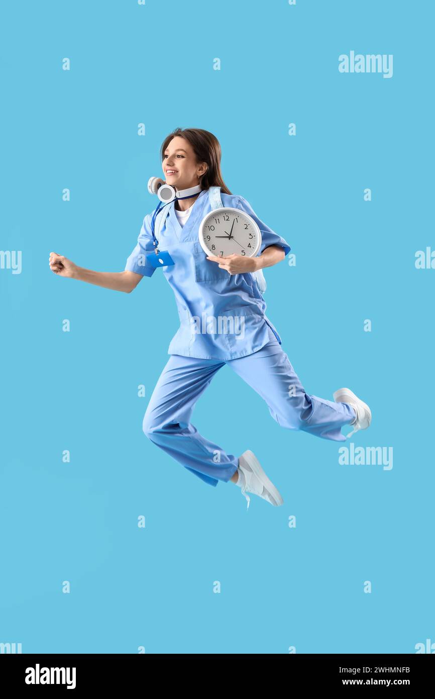 Female medical intern with clock jumping on blue background Stock Photo ...