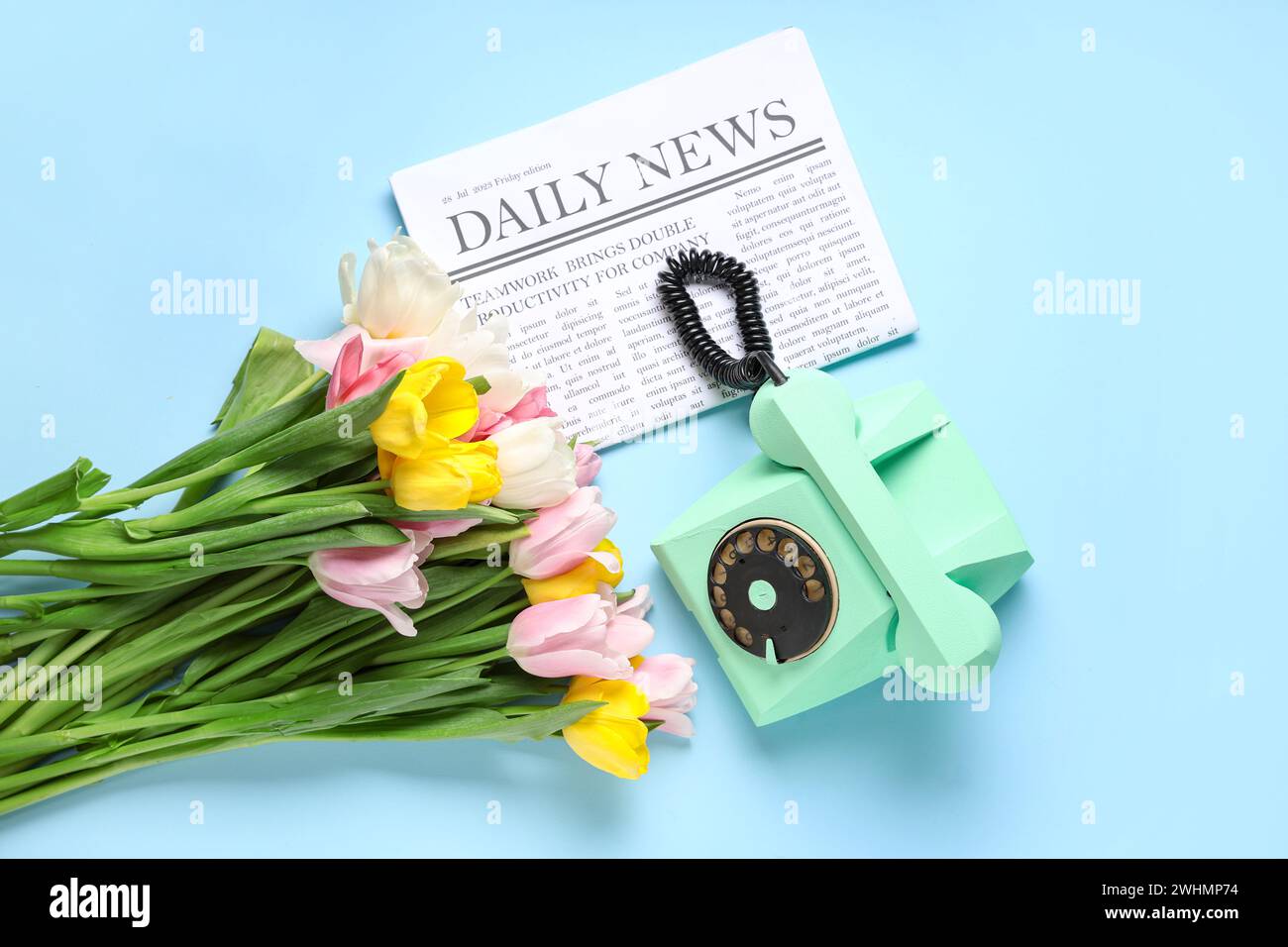 Retro telephone with bouquet of beautiful tulips and newspaper on blue ...